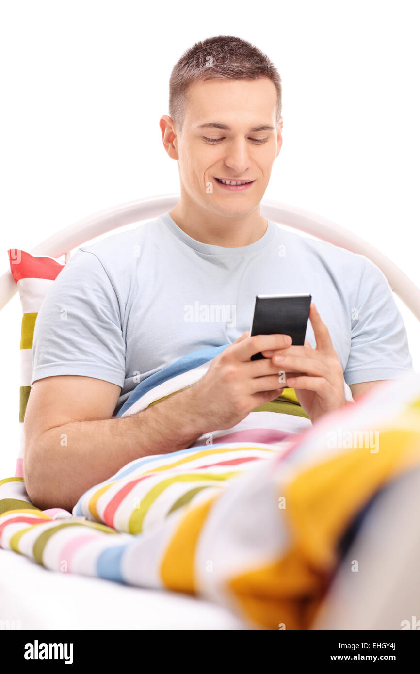 Young man texting someone from his cell phone and lying in bed isolated ...