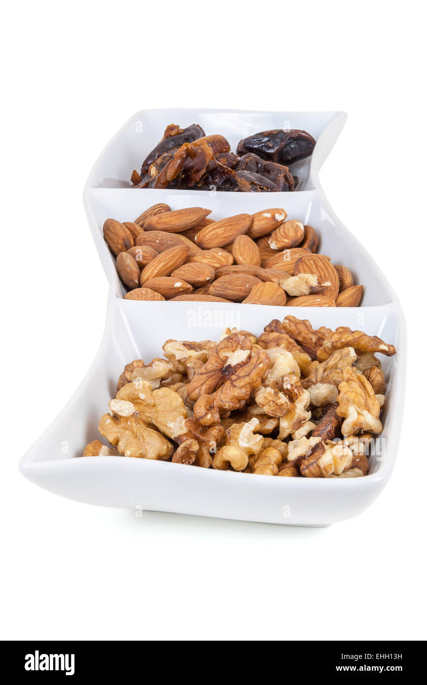 Walnuts almonds and dates in a white dish isolated on white background ...