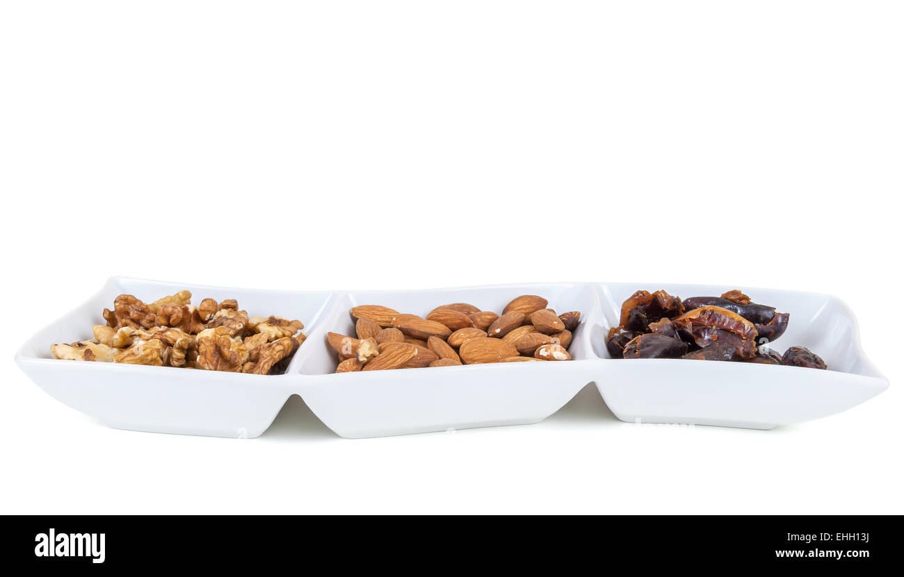 Walnuts almonds and dates in a white dish isolated on white background ...