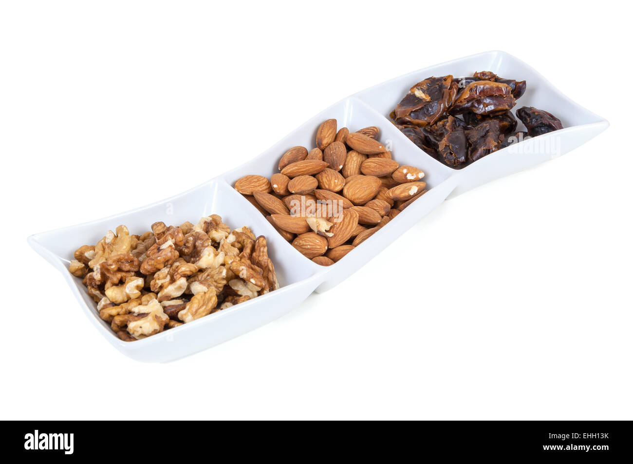 Walnuts almonds and dates in a white dish isolated on white background ...
