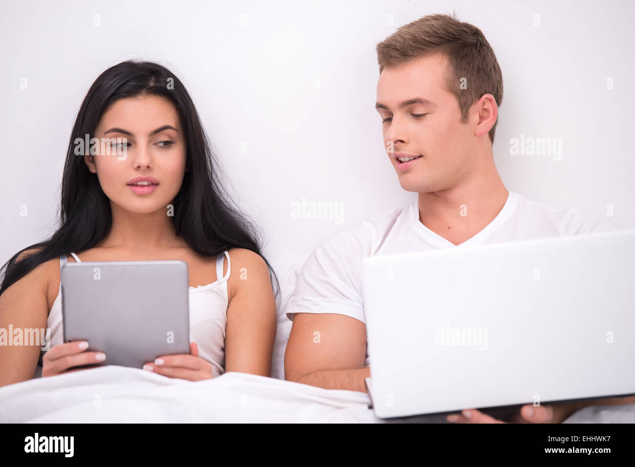 Man and woman looking at each other's computers while sitting in bed ...