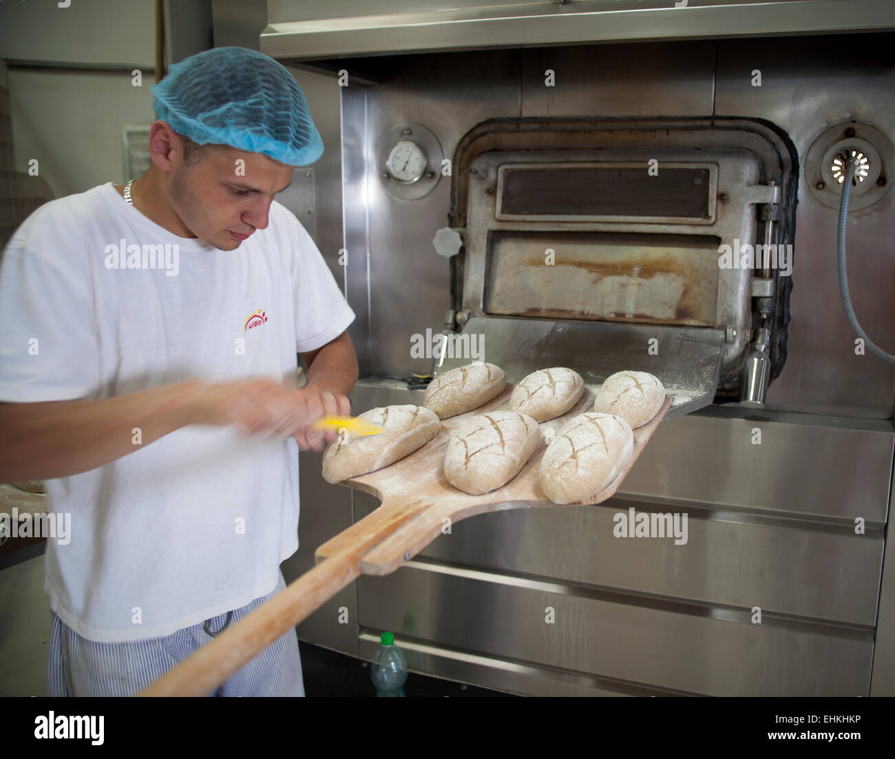 Baker preparing loaves of bread on paddle before placing in the oven ...