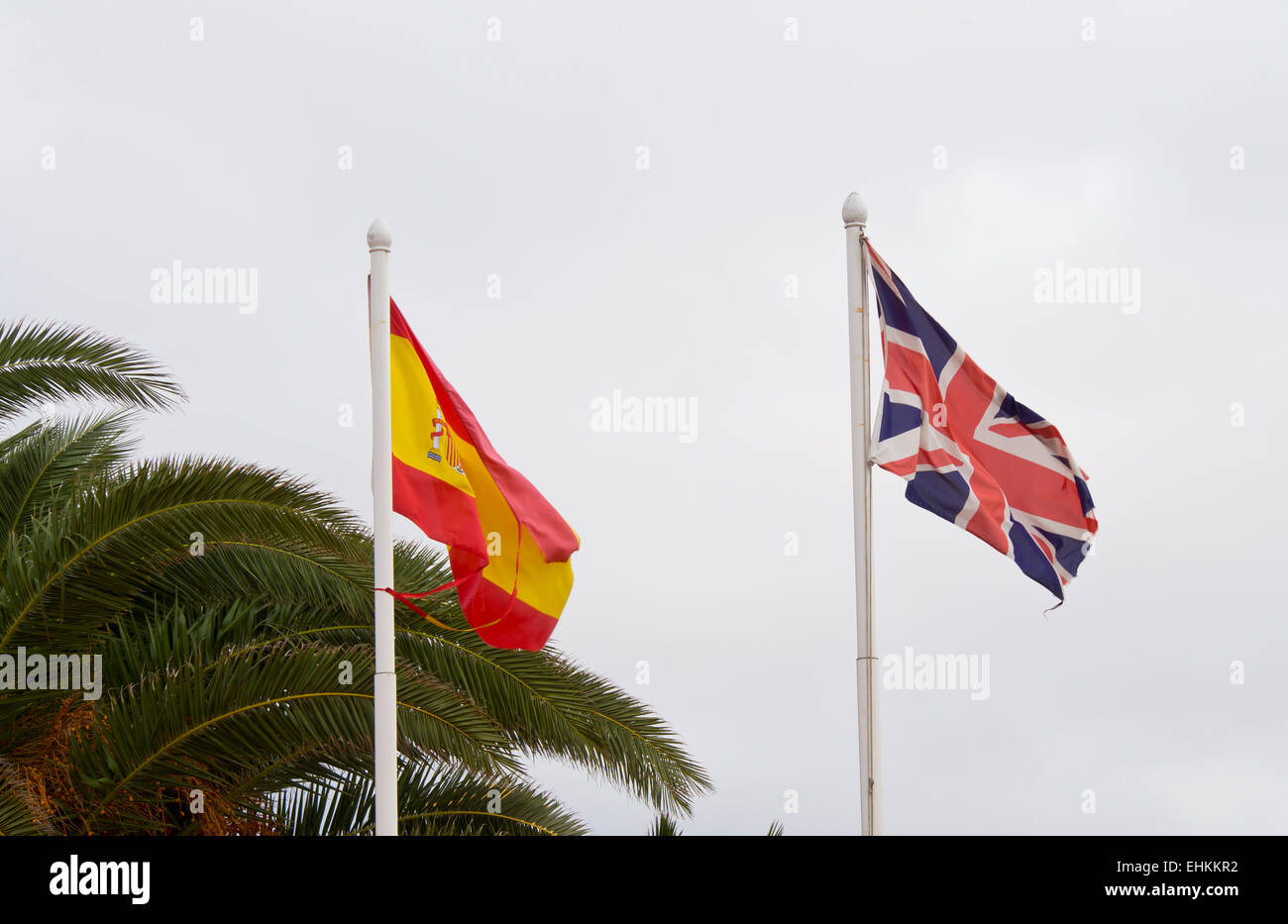 Union Jack and Spanish flag on flagpoles with palm tree leaves ...