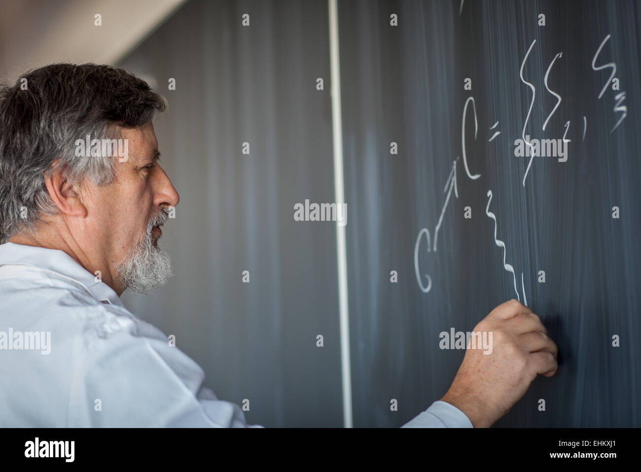 Senior chemistry professor writing on the board while having a chalk ...
