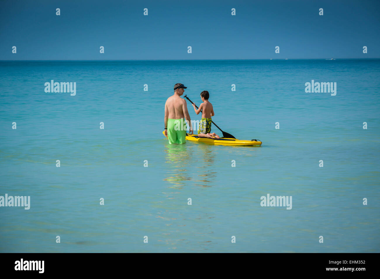 Father oversees son's attempt at paddle boarding in the shallow and ...