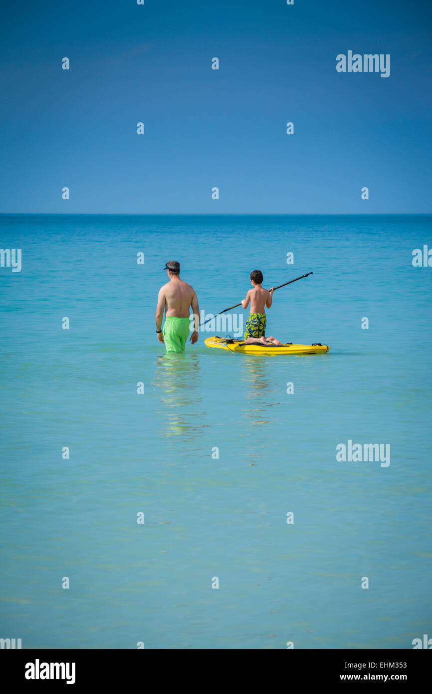 Father oversees son's attempt at paddle boarding in the shallow and ...
