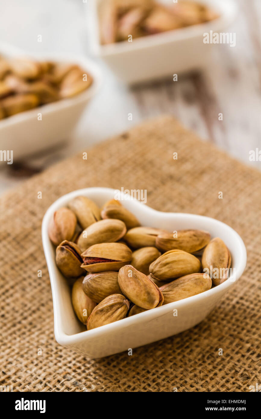 Pistachio nuts in heart shaped ceramic bowls on white wooden background ...