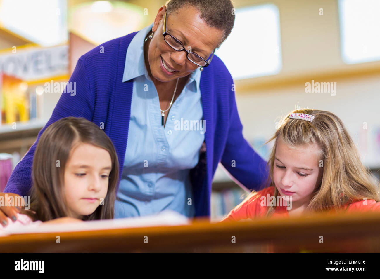 Teacher helping students in library Stock Photo - Alamy