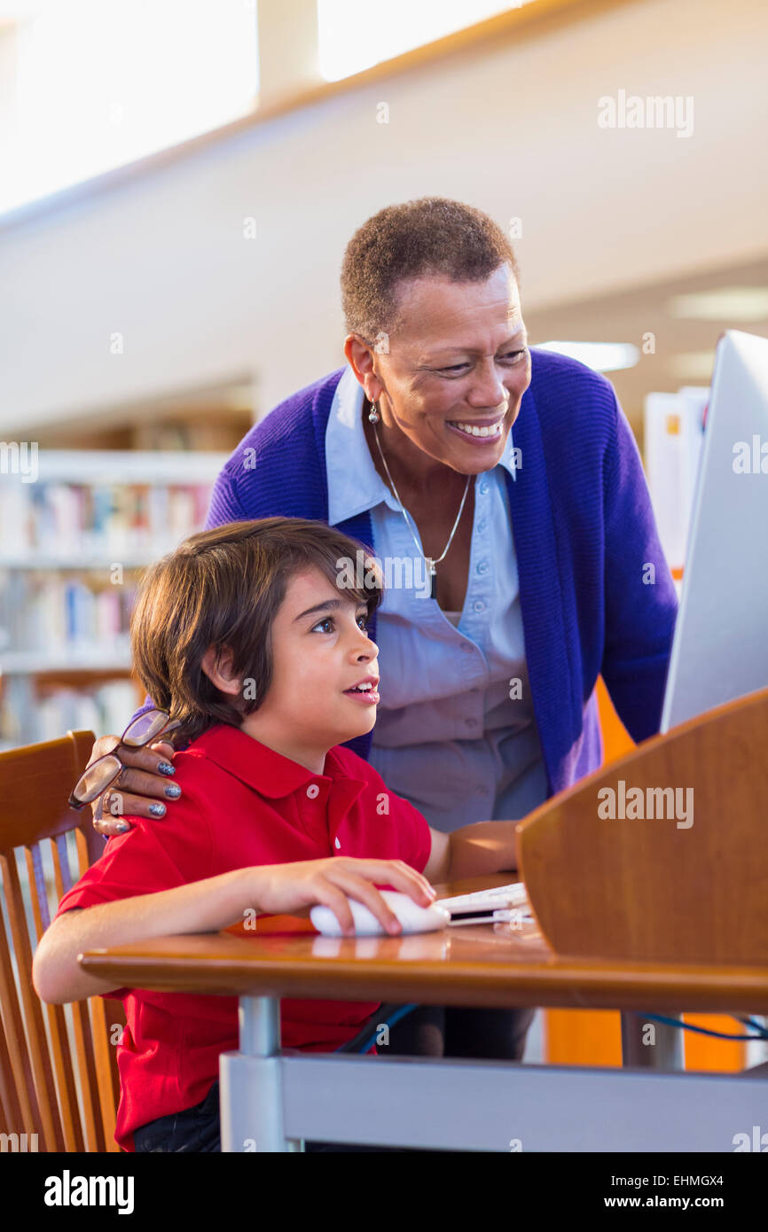 Teacher helping student use computer in library Stock Photo - Alamy