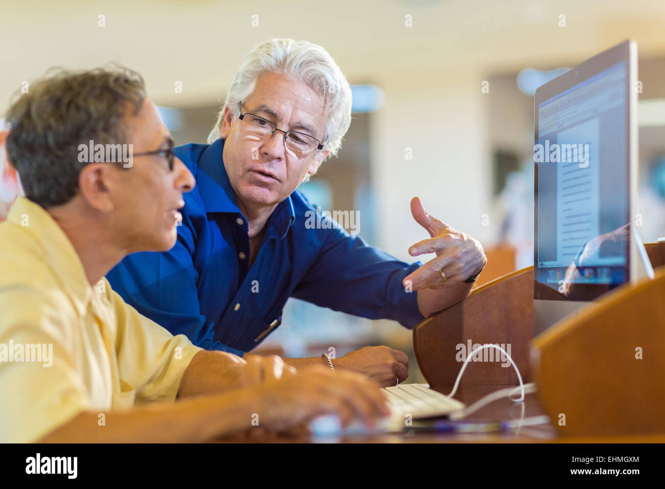 Teacher helping adult student use computer in library Stock Photo - Alamy