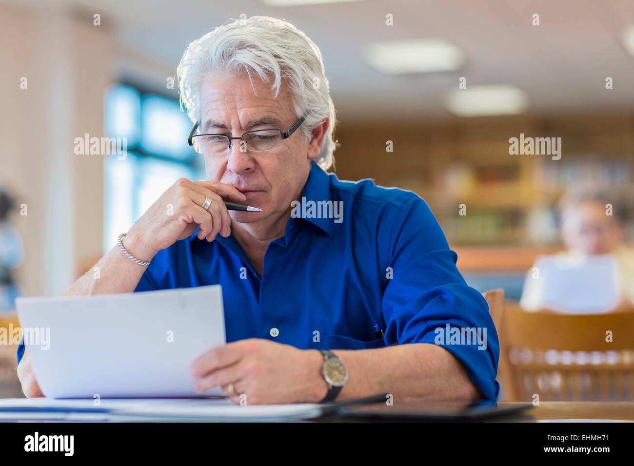 Man reading paperwork in library Stock Photo - Alamy