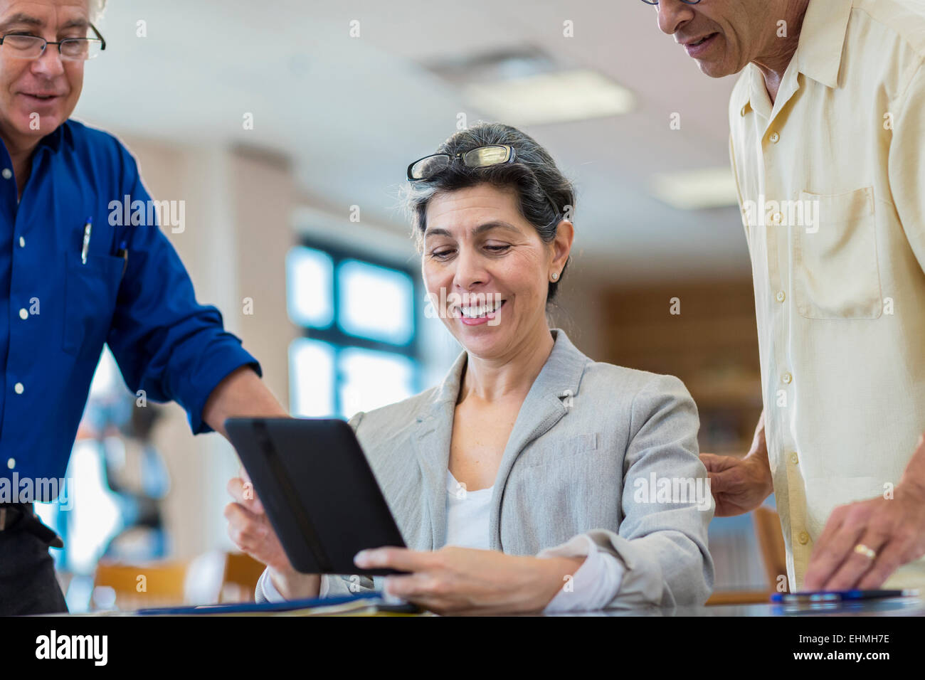 Teacher helping adult students use digital tablet in library Stock ...