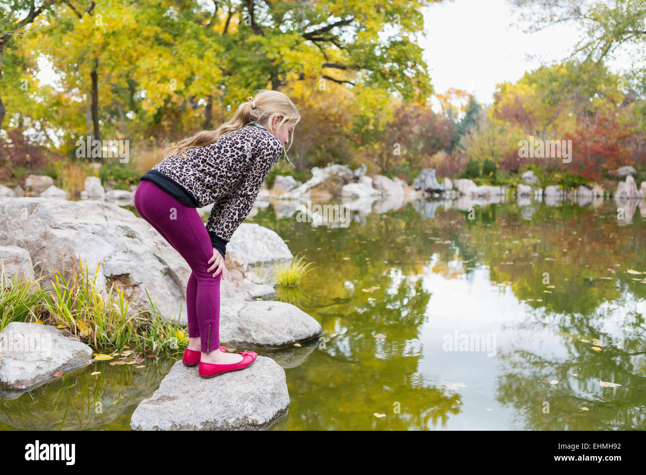 Caucasian girl crouching on rock in pond Stock Photo - Alamy