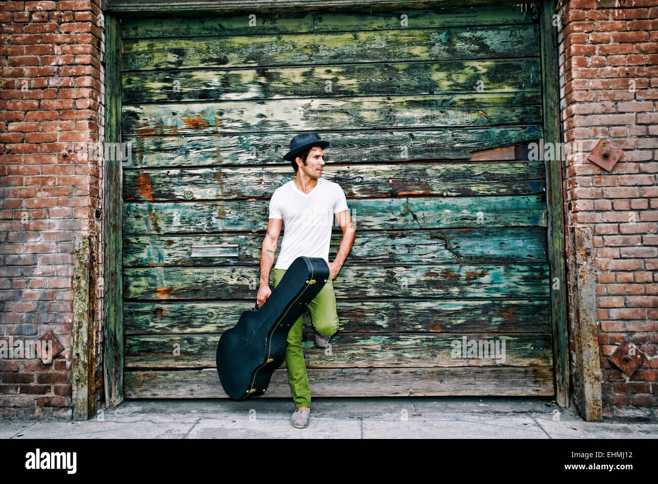 Mixed race musician holding guitar case near industrial building Stock ...