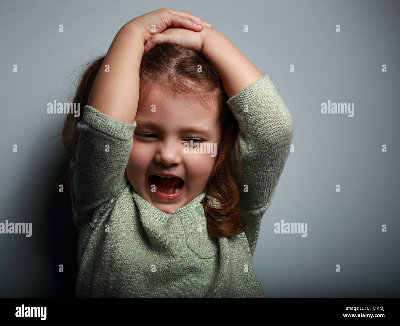Angry kid girl shouting with open mouth and holding hands the head on ...