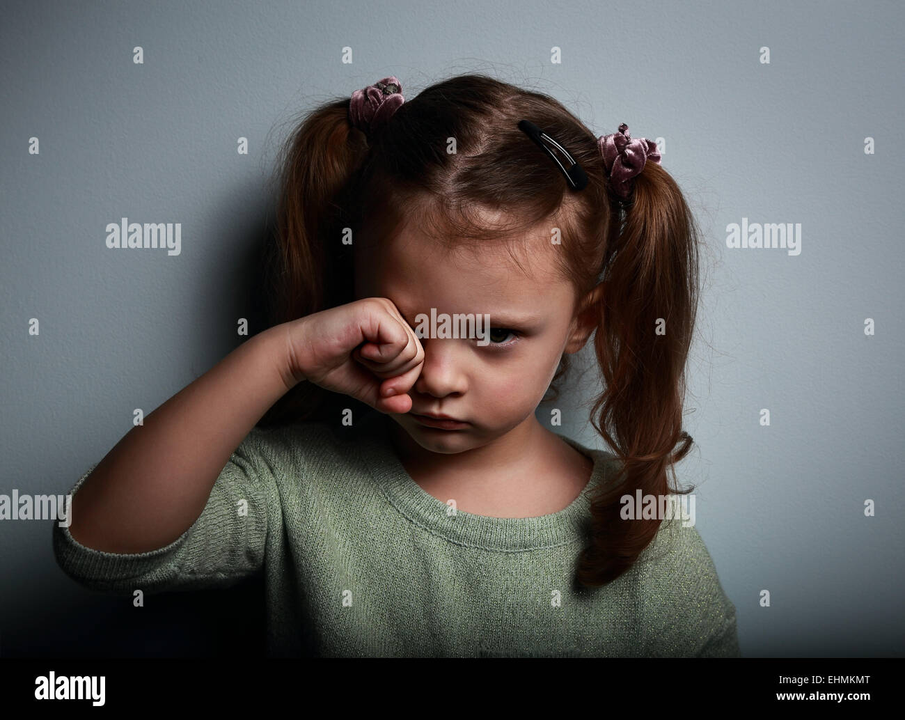 Crying kid girl with hand near eyes looking unhappy on dark background ...