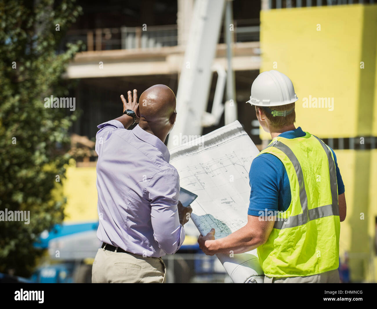 Businessman and construction worker reading blueprints at construction ...