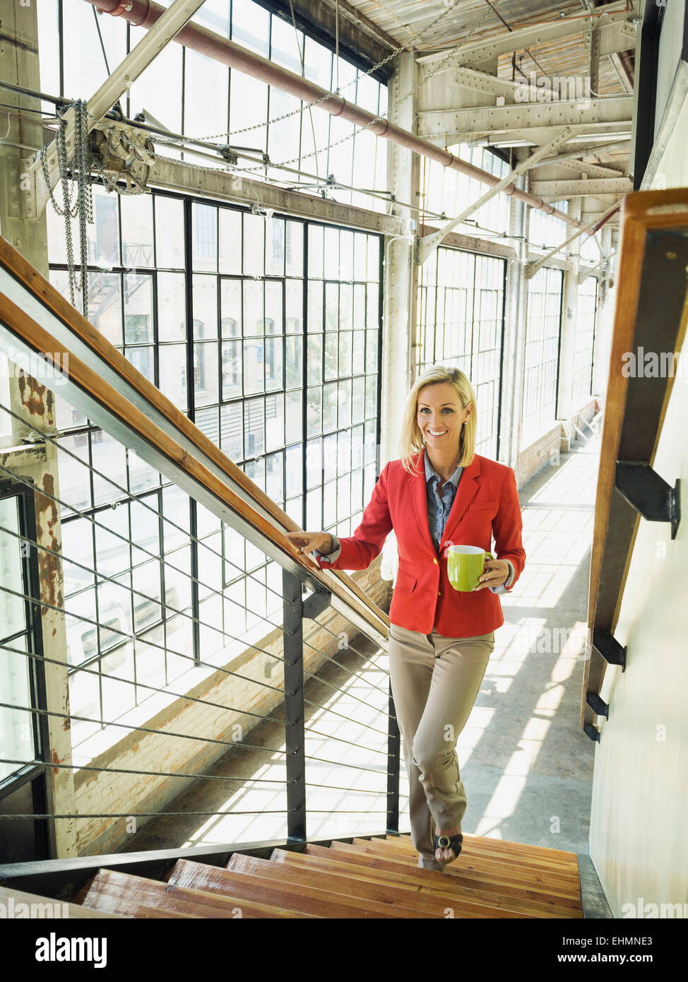 Caucasian businesswoman carrying cup of coffee on warehouse staircase ...