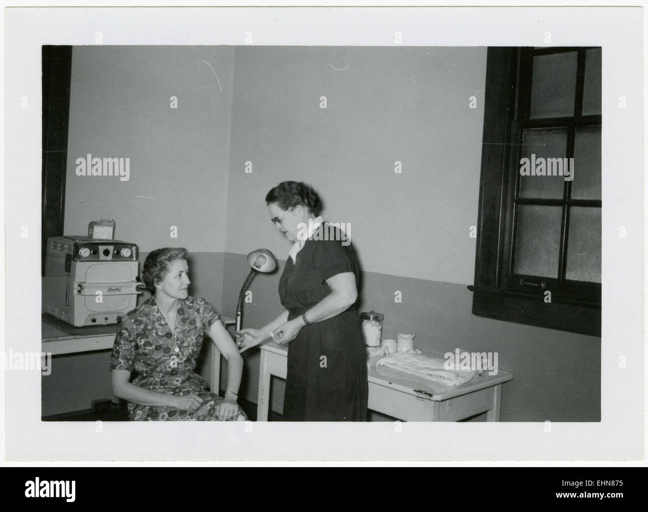 This 1940s image captures a nurse assisting a young woman at a table ...
