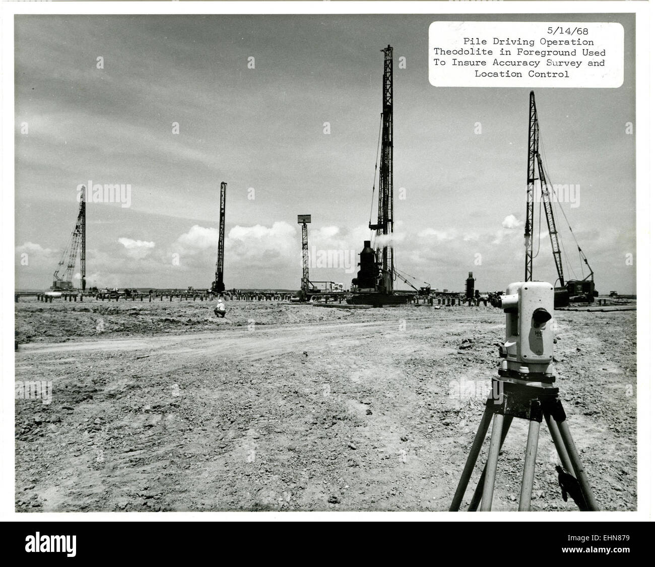 This photograph depicts a pile driving operation, with a theodolite in ...