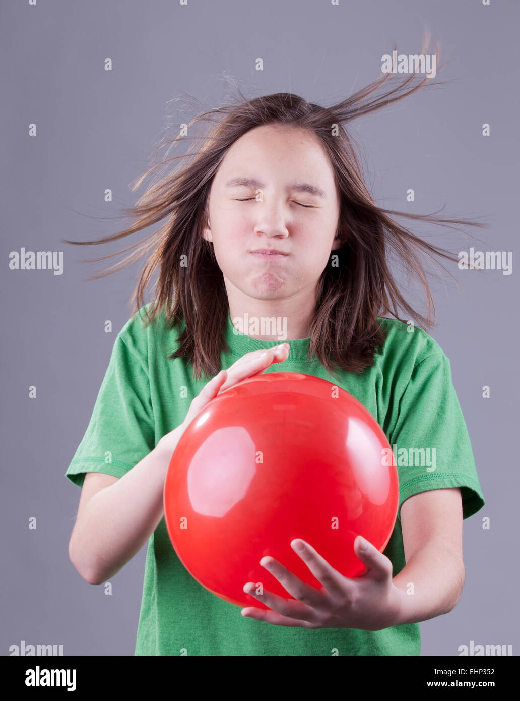 A young girl lets the blast of air from a balloon mess up her hair ...