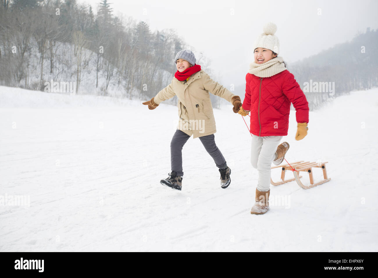 Happy children running with sled on the snow Stock Photo - Alamy