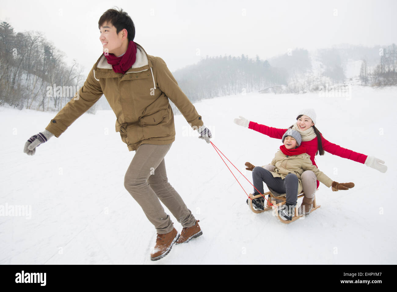 Happy family playing with sled on the snow Stock Photo - Alamy