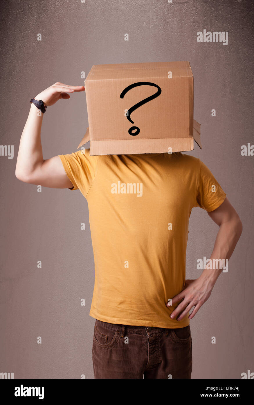Young man gesturing with a cardboard box on his head with question mark ...