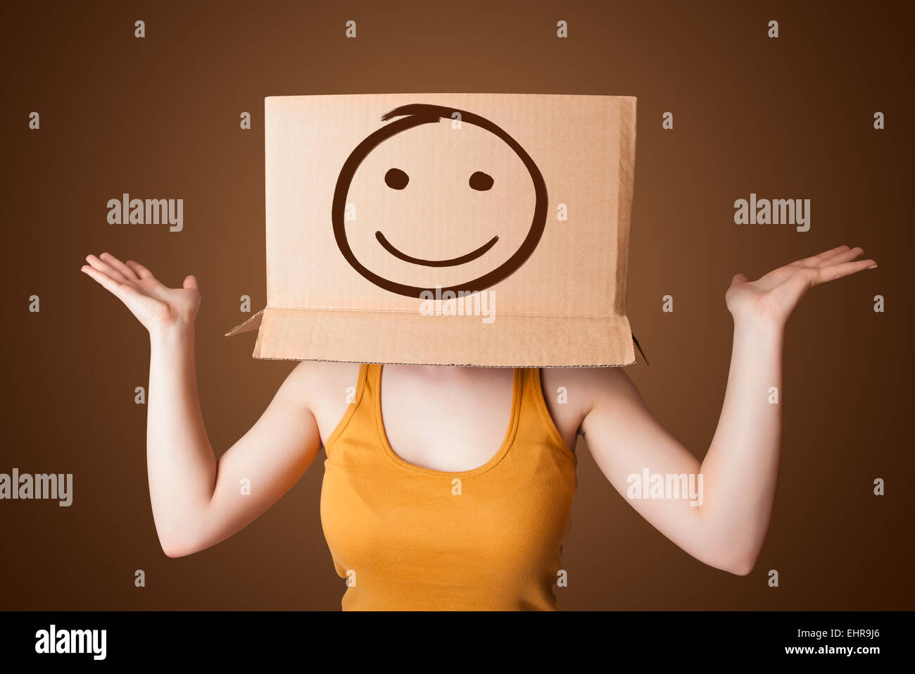 Young girl gesturing with a cardboard box on her head with smiley face ...