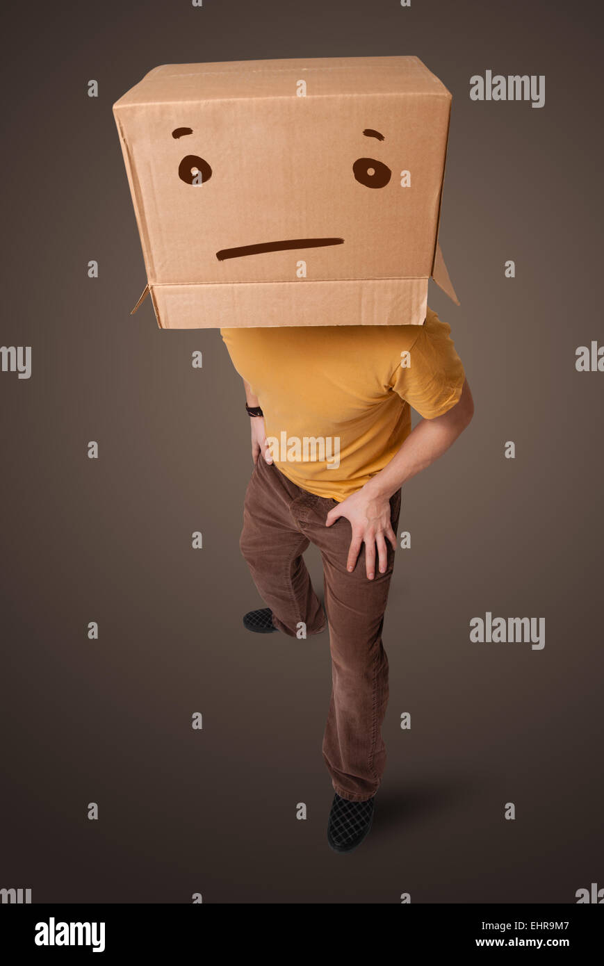 Young man gesturing with a cardboard box on his head with straight face ...