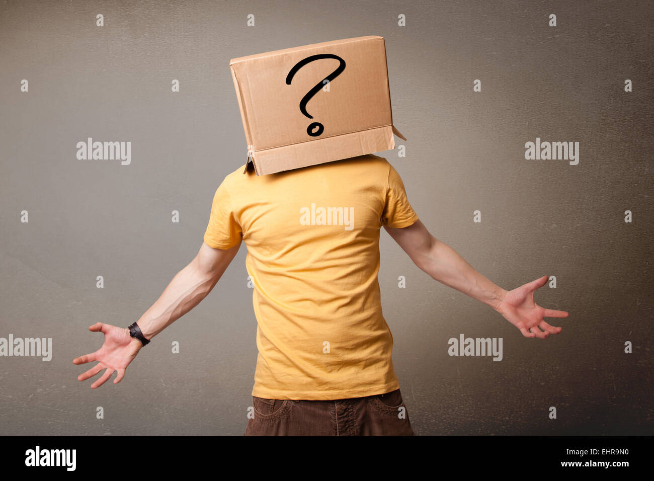 Young man gesturing with a cardboard box on his head with question mark ...