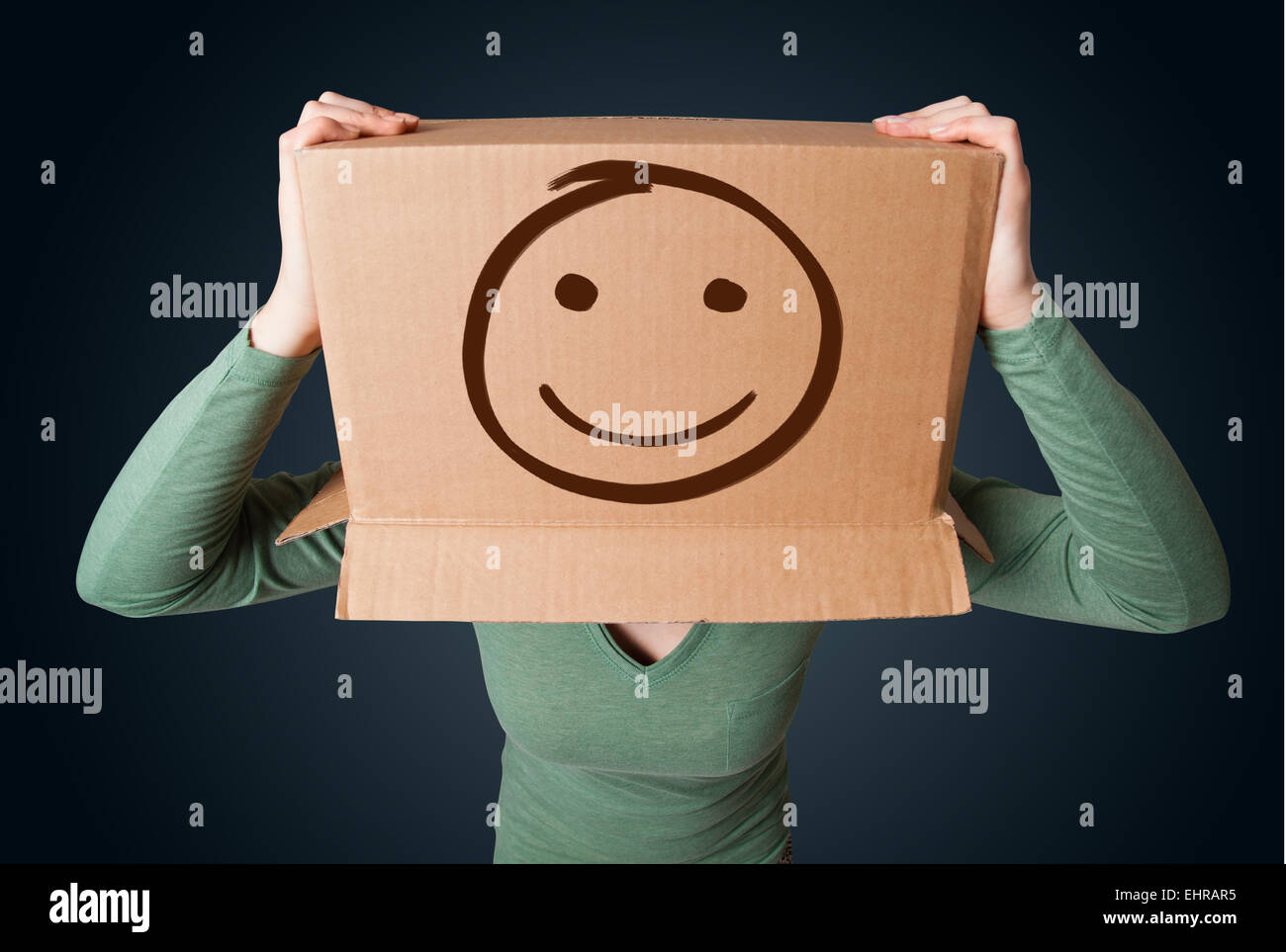 Young girl gesturing with a cardboard box on her head with smiley face ...