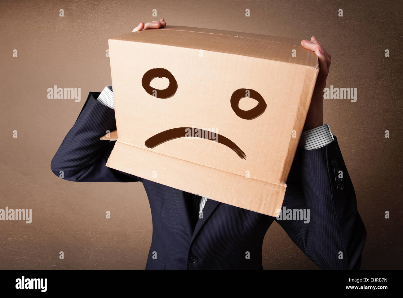 Businessman gesturing with cardboard box on his head with sad face ...