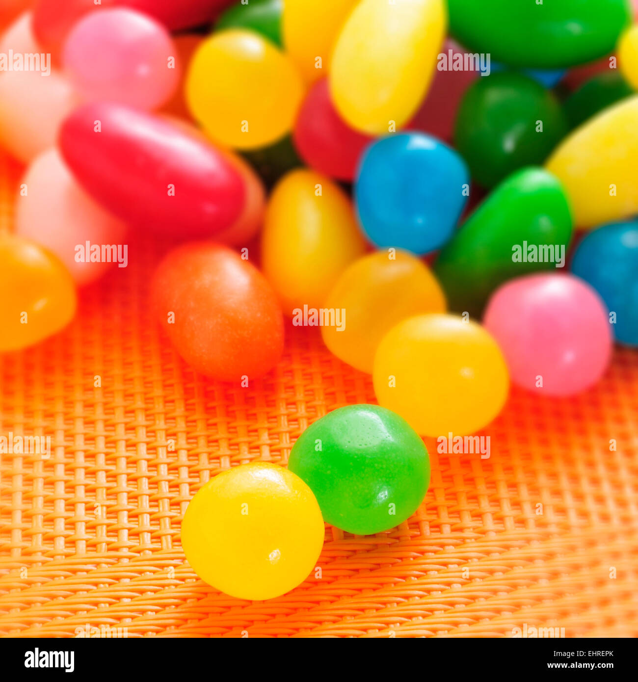 a pile of jelly beans of different colors on an orange woven background ...