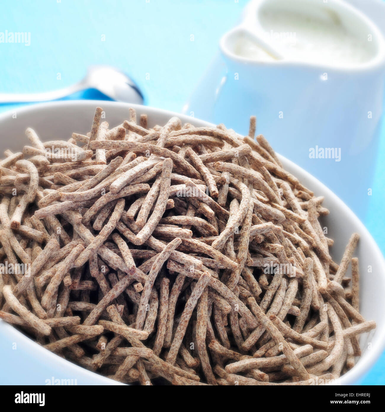 closeup of a bowl with cereal bran sticks and a milk pot on a blue ...