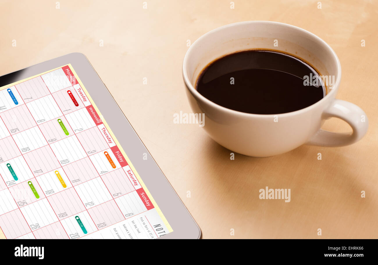 Tablet pc showing calendar on screen with a cup of coffee on a desk ...