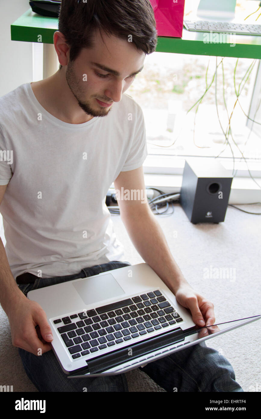 Man looking down at laptop next to window Stock Photo - Alamy