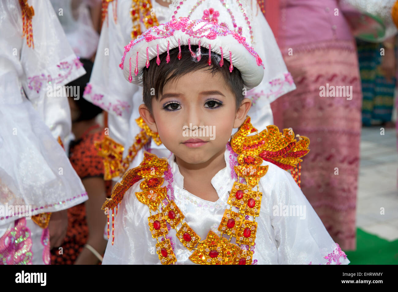 A young Burmese boy dressed in colourful robes and doll like make up ...