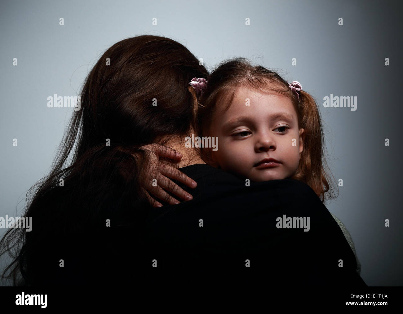 Small sad daughter hugging her mother with love on dark background ...