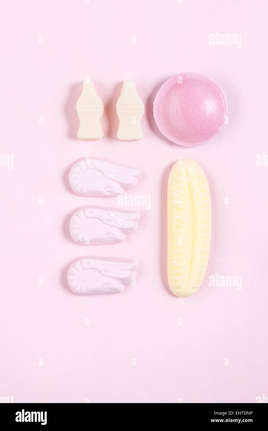 Colour coordinated sweets laid out and organised on a light pink ...