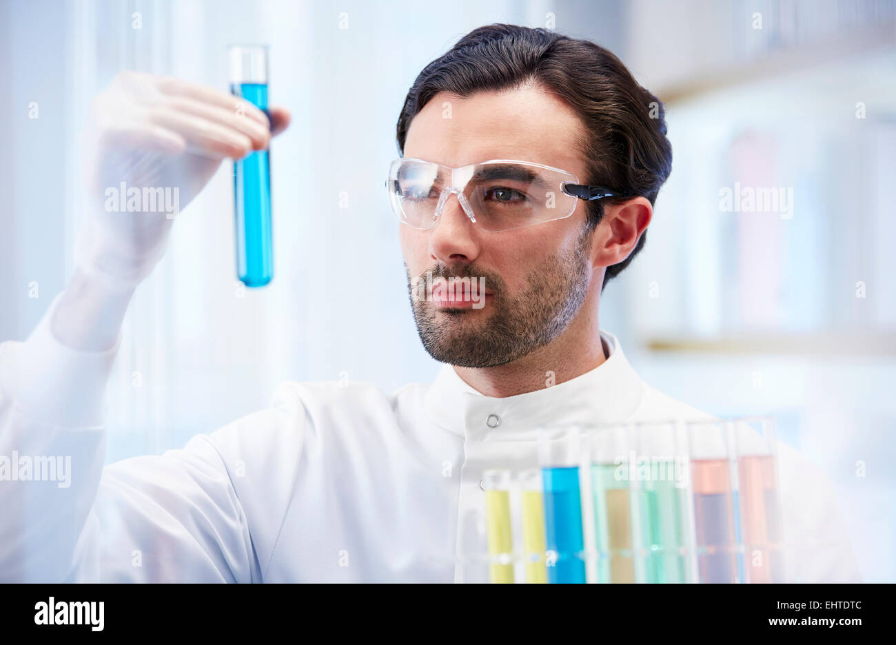 Man in laboratory looking at vial with blue fluid Stock Photo - Alamy