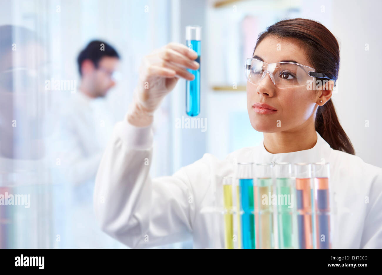 Woman in laboratory looking at vial with blue fluid Stock Photo - Alamy