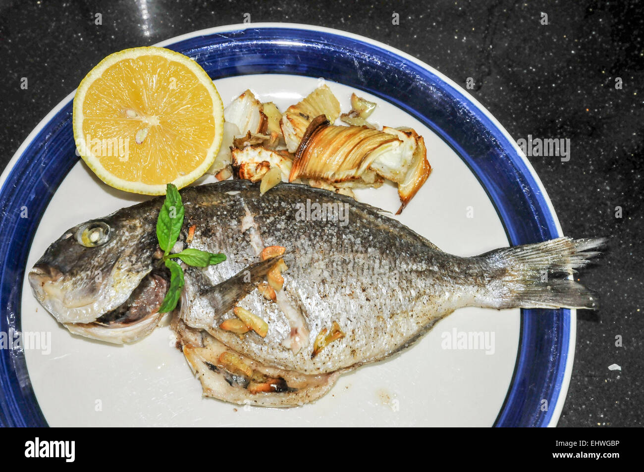 a plate with a Grilled fish with garlic and lemon Stock Photo - Alamy