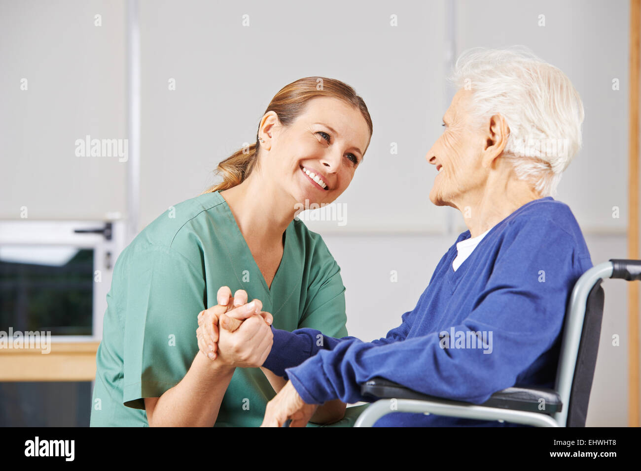 Happy geriatric nurse holding hands with senior woman in a wheelchair ...