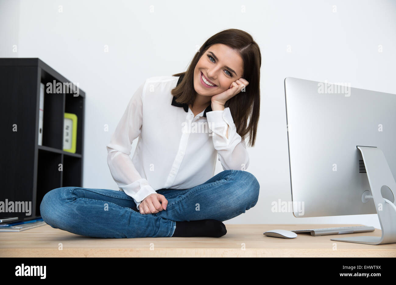 Smiling young businesswoman sitting on the table in office Stock Photo ...