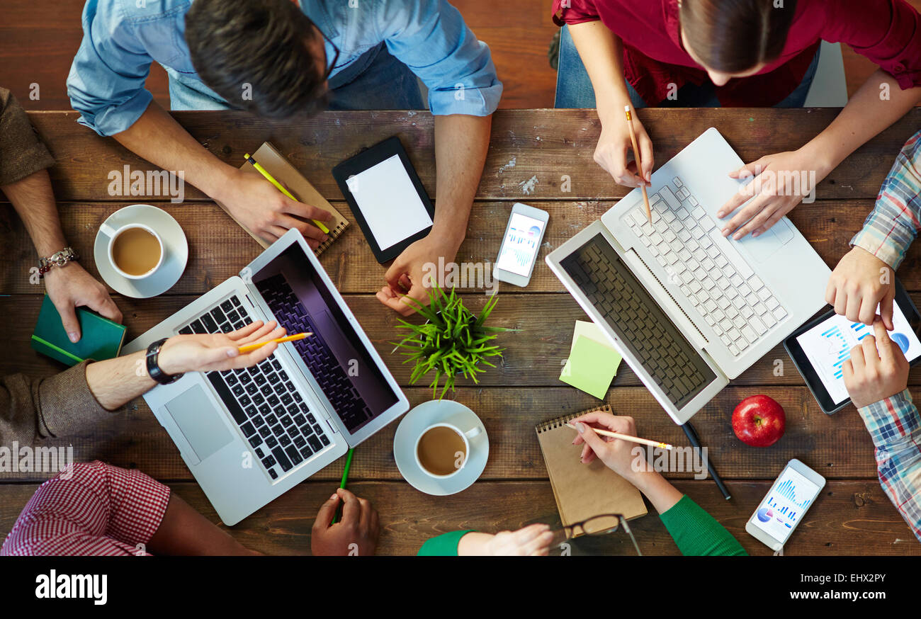 High angle view of people meeting at table and working with laptops and ...
