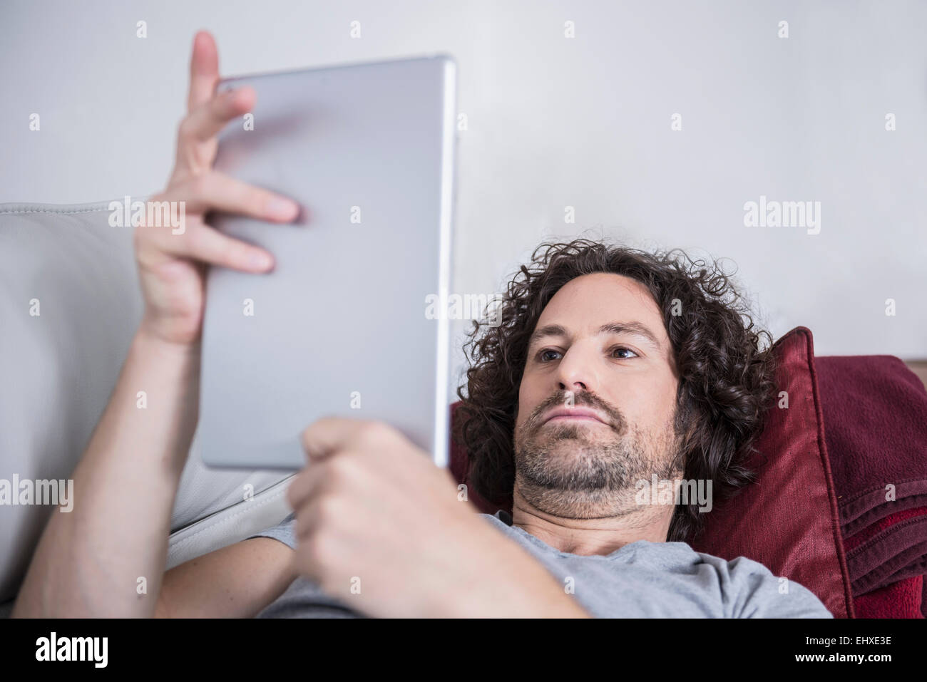 Man lying down on couch and using a digital tablet, Munich, Bavaria ...