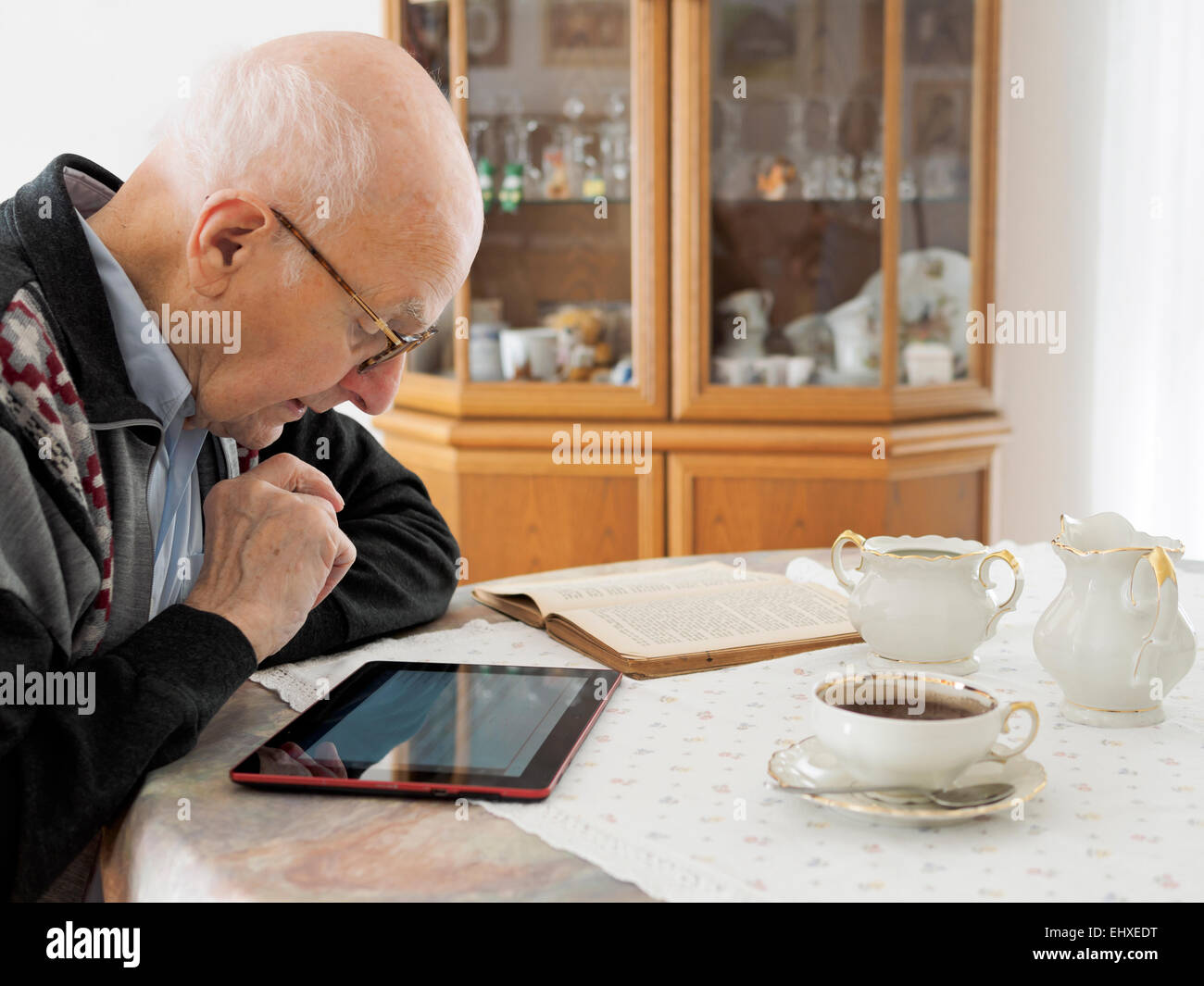 Old man sitting at table using digital tablet Stock Photo - Alamy