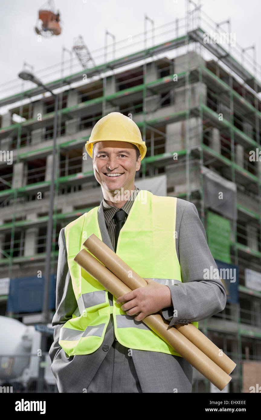 Portrait of a happy male site manager standing with blueprints at a ...