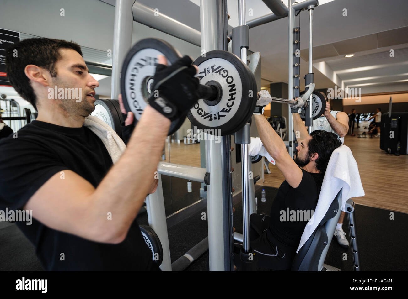 Man putting a weight plate on the bar for another man to lift at the ...